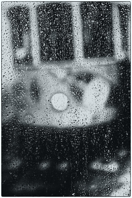 Rain on windshield: grayscale, abstract glimpse of an urban scene through rain-slick glass