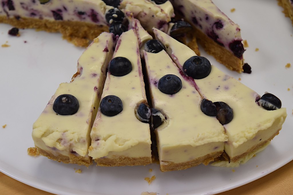 Blueberry cheesecake bars with creamy filling on a golden biscuit crust, sliced and arranged on a white plate