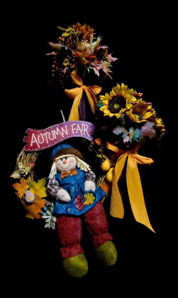 Autumn Fair Display: Sunflowers, Leaves, and a Fabric Scarecrow Doll Against a Black Backdrop