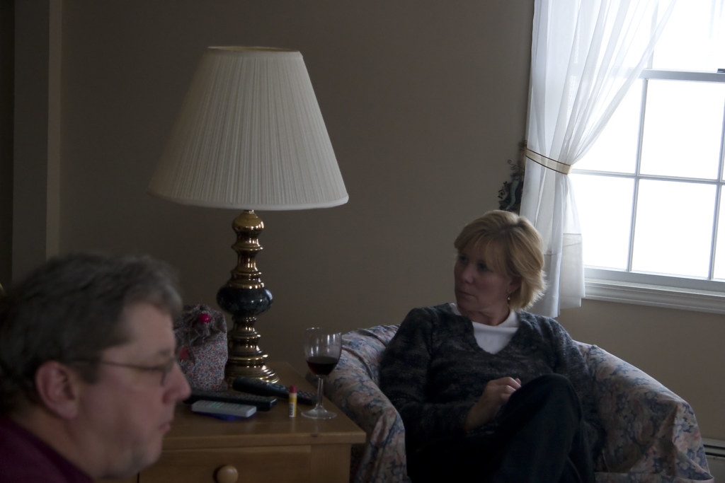 Conversation in a Cozy Living Room: Woman in Floral Chair by Window, Man in Foreground