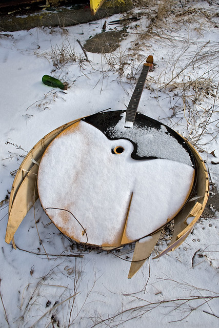 Snow-covered round-bodied guitar abandoned in an urban ruin