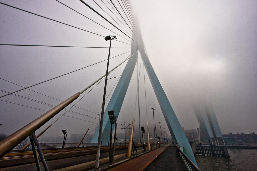 Fog-enshrouded cable-stayed bridge: blue arches loom through the morning mist
