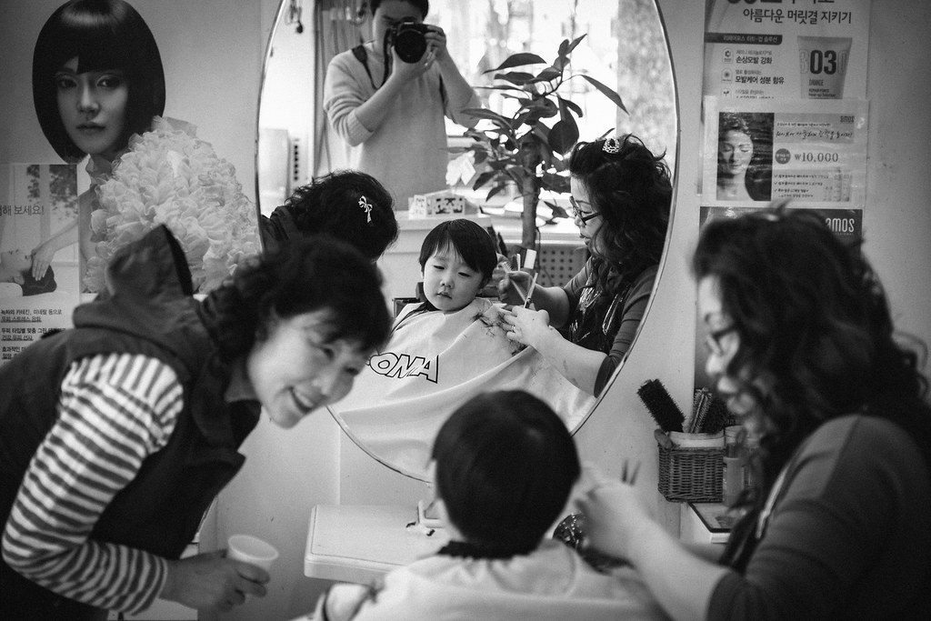 원형 거울 속 아이의 커트 순간과 바쁜 미용실의 풍경