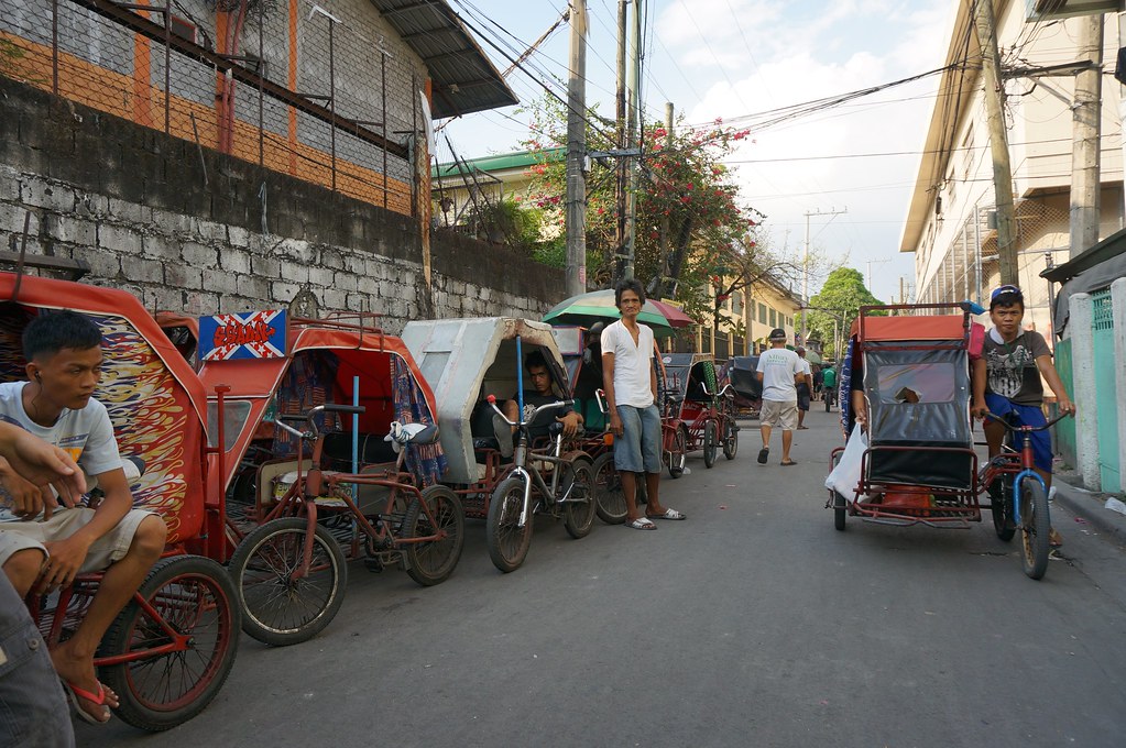 Colorful tricycles line a sunlit Philippine street with locals along an urban lane