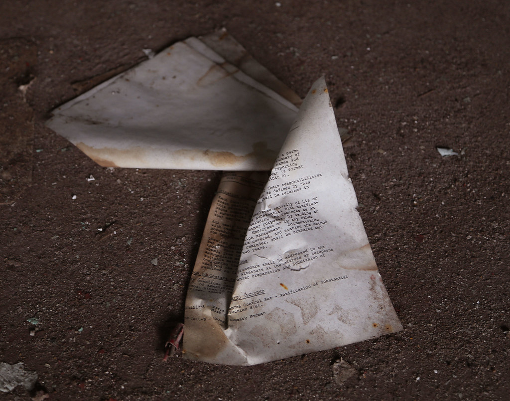 Crumpled typed document on a dusty floor with folded corners and stains