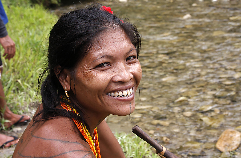 Mentawai Islands portrait: smiling woman by a rocky riverbank wearing orange bead necklace