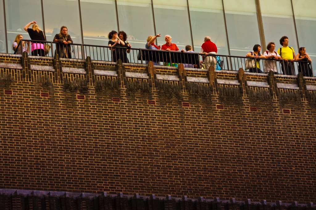 Tate Modern Balcony: Diverse visitors along a brick terrace beneath a glass atrium