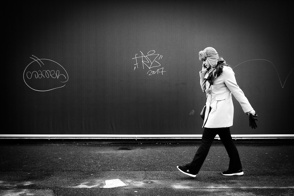 Berlin Winter Street Portrait: Woman in a pale coat strides past graffiti on a rain-darkened wall (2017)