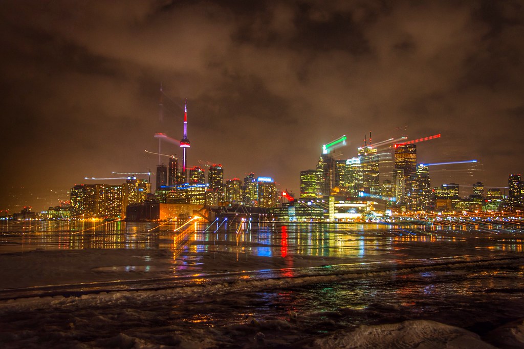 Toronto Waterfront Nightscape: CN Tower, Crane Light Trails, and Reflections on a Wet Promenade