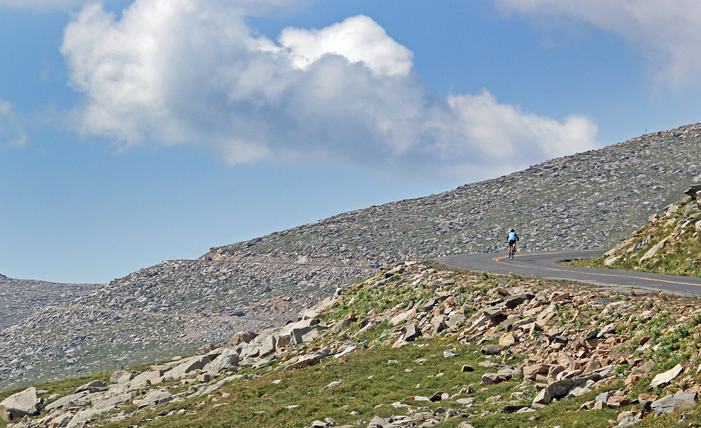 Cyclist on Mount Evans' Highest Paved Road, Colorado: Alpine ascent along a rocky slope under blue skies