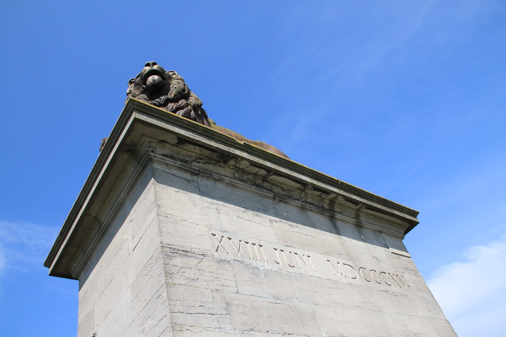 Lion's Mound, Waterloo Battlefield: Stone pedestal topped by a lion sculpture beneath a clear blue sky