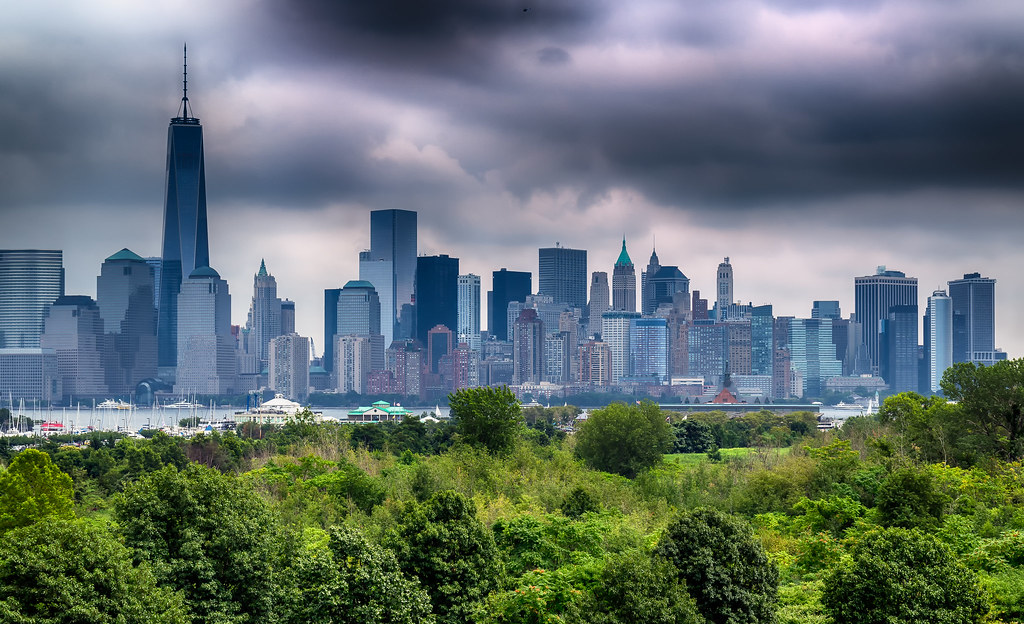 Storm-Clouded Manhattan Skyline: One World Trade Center Rises Over a Lush Foreground