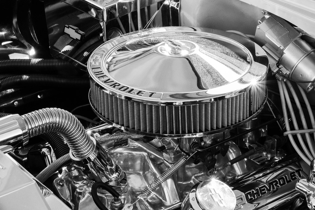 Chevrolet V8 engine bay: chrome round air cleaner centerpiece amid braided hoses and polished components (black-and-white study)