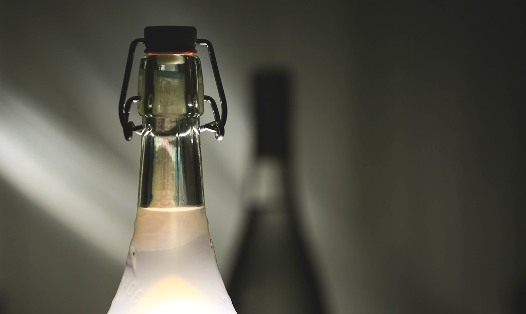 Close-up of a swing-top glass bottle, lit from the side, with a softly blurred background bottle