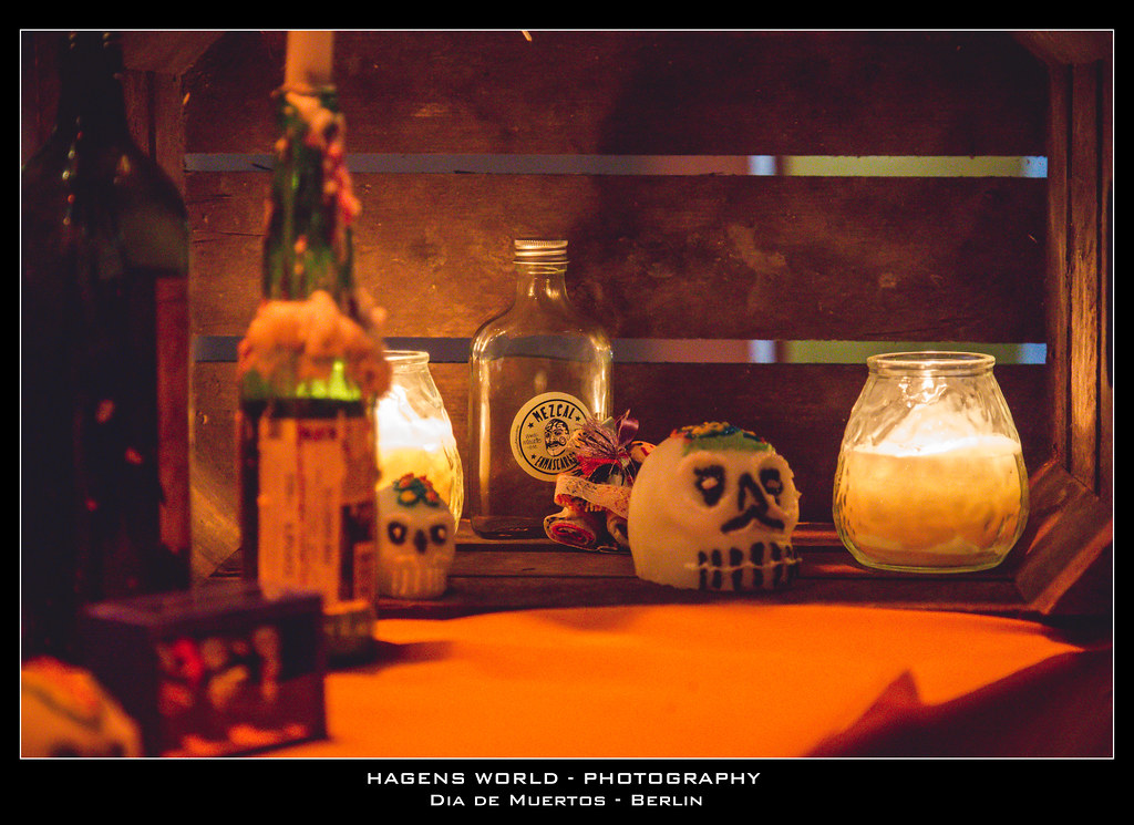 Dia de Muertos altar in Berlin: candlelit sugar skulls and a mezcal bottle on a wooden shelf