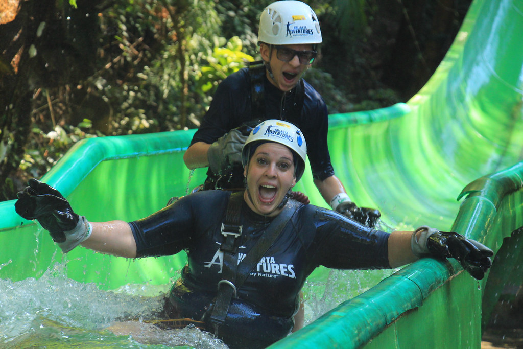 Green Water Slide Descent: Two helmeted riders capture a splashy, outdoor adventure moment
