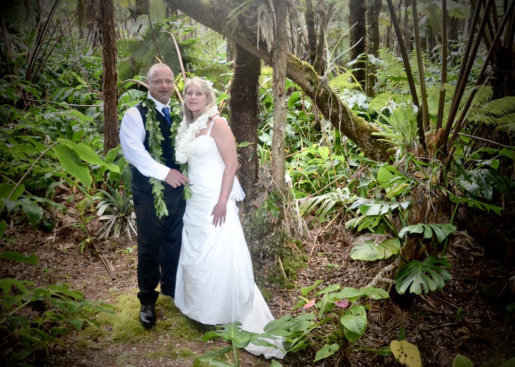 Tropical Jungle Wedding Portrait: Bride in a white gown and groom in formal attire among lush tropical foliage