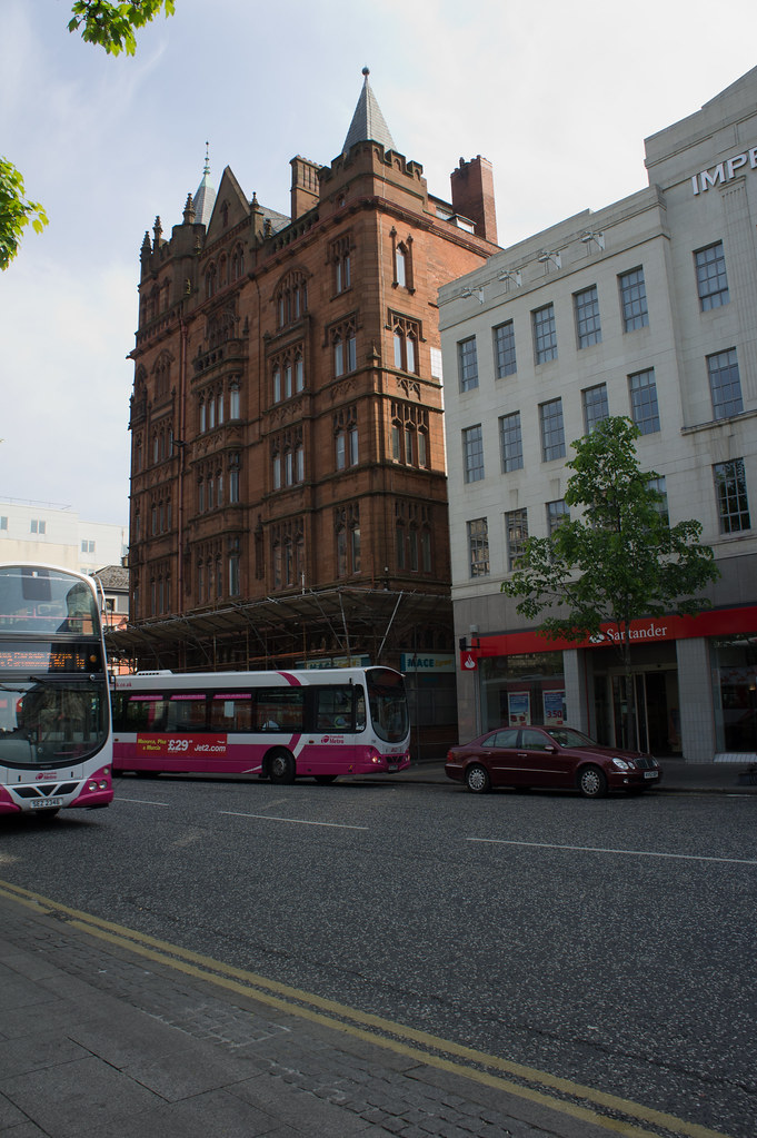 Donegall Square, Belfast: Ornate red-brick building beside a modern storefront with a pink city bus in the foreground