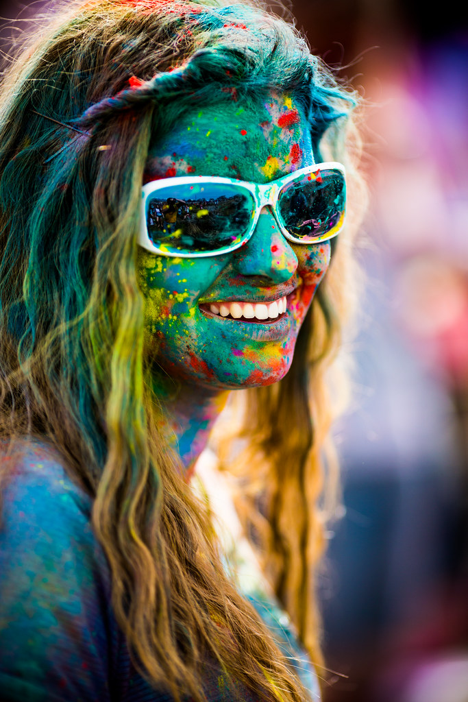 Colorful Holi Portrait: Smiling woman with powder-splashed skin and white sunglasses
