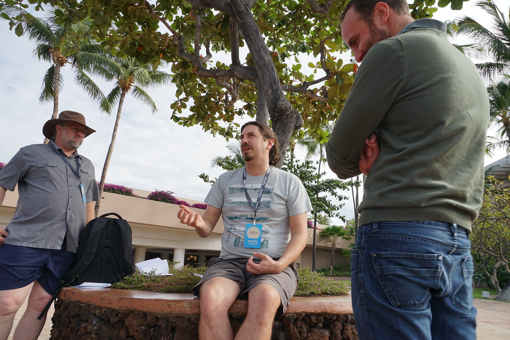 Casual conference break in a tropical courtyard: three men converse by a planter under palm trees