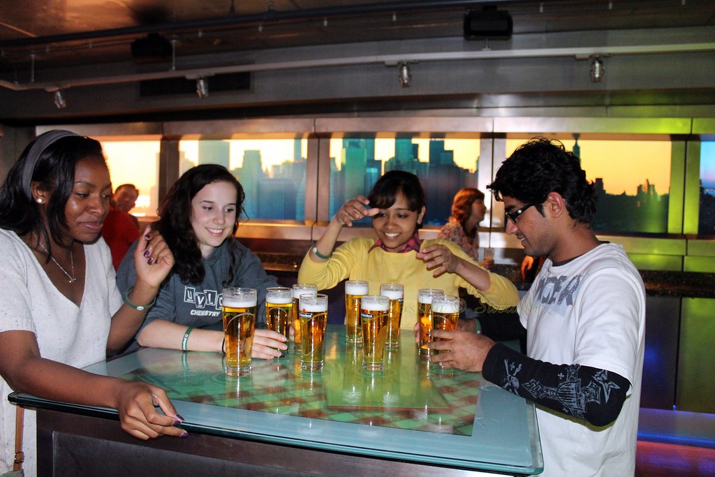 Friends toast at a glass-topped bar with a glowing skyline backdrop