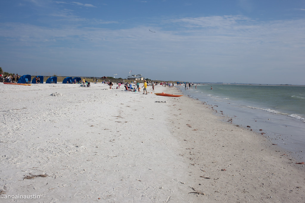 Crowded White-Sand Beach with Blue Tents, Turquoise Water, and an Orange Kayak along the Shore