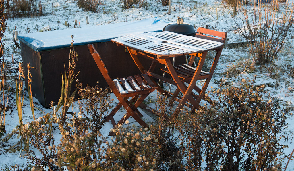 Winter sunlight illuminates a wooden folding patio set in a snow-dusted Helsinki garden