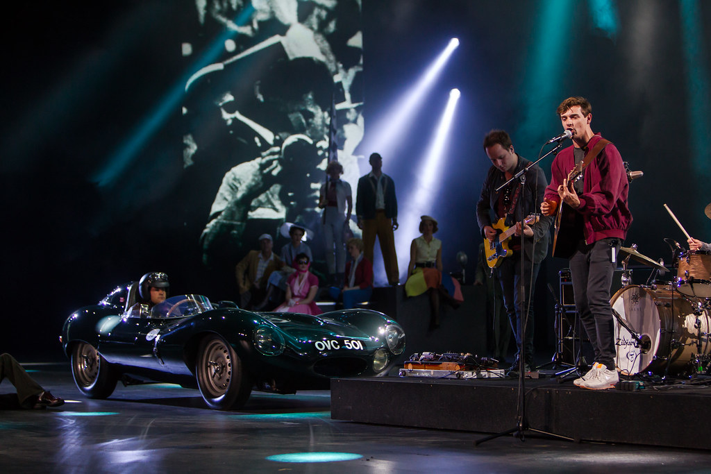 Classic green Jaguar race car on stage beside a live band during a London event