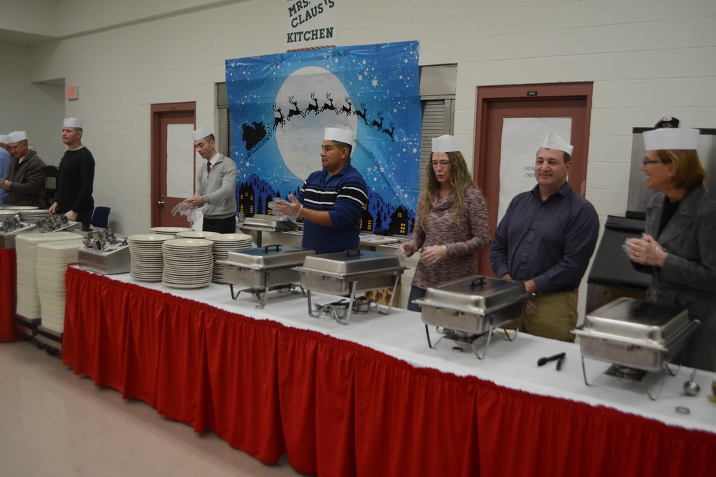Holiday Dinner Service at Mrs. Claus's Kitchen: Volunteers Prepare Meals Behind a Red-Skirted Serving Table