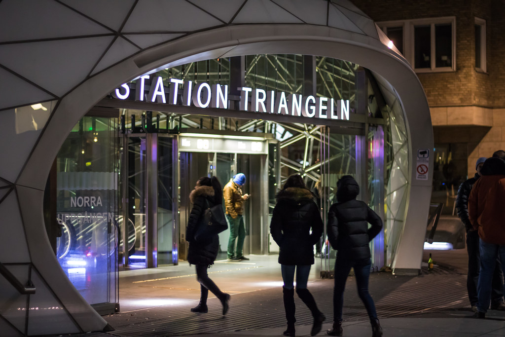 Triangeln Station Entrance at Night: Glass Archway, Neon Lighting, and Pedestrians in Winter Coats