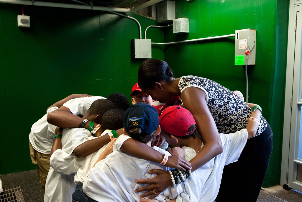 Mentor leads a close-knit group hug with children in a green-walled indoor space, capturing a moment of care.