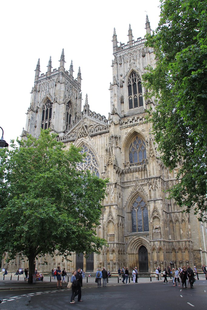 York Minster's intricate Gothic facade with two towering spires, surrounded by trees and visitors.