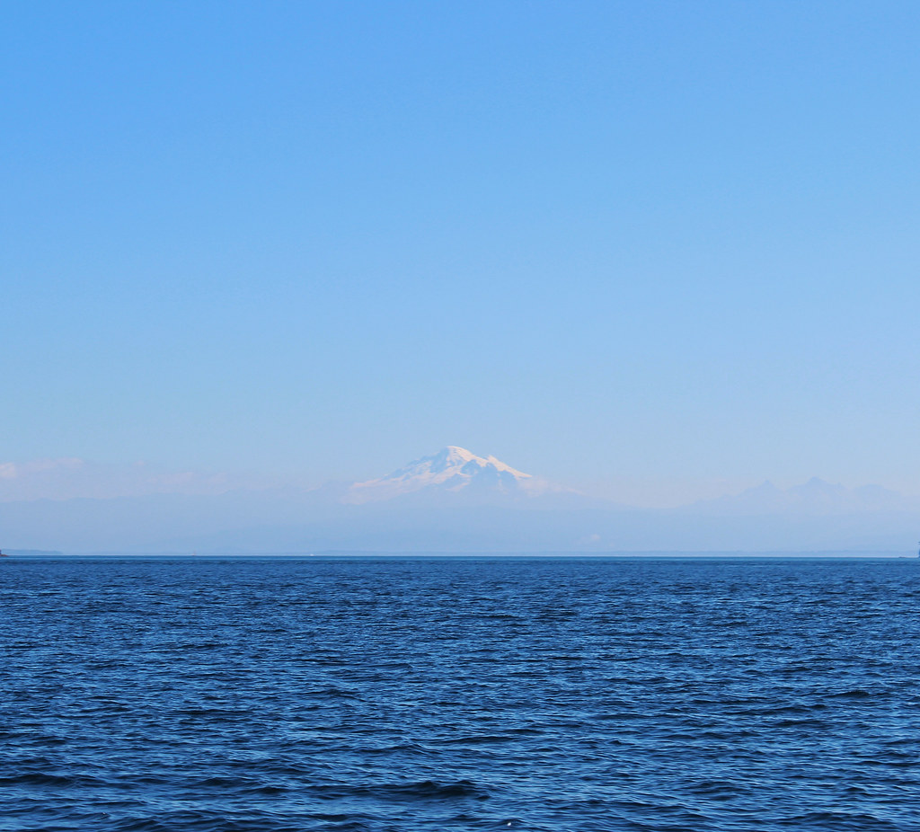 Salish Sea Vista: Distant Snow-Capped Peaks of Cascade and Olympic Ranges Across Calm Coastal Waters