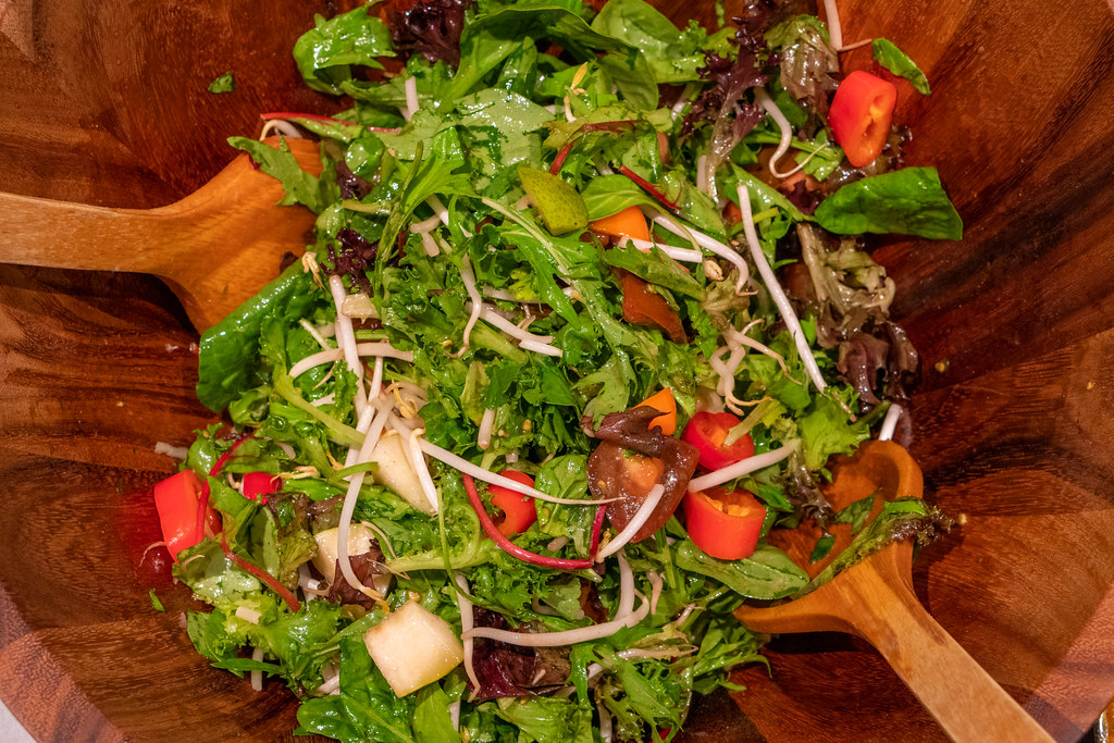 Top-down view of a colorful mixed greens salad with bean sprouts and bell peppers in a wooden bowl