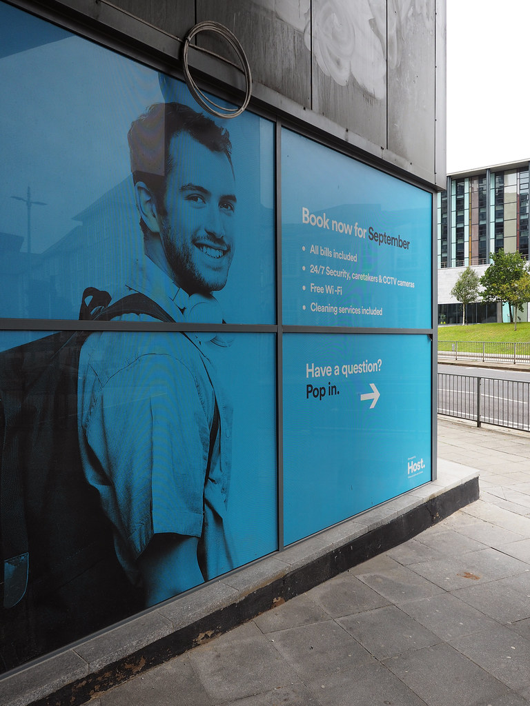 Blue promotional storefront window with a smiling man and 'Book now for September' offer