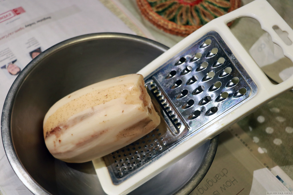 Lotus root resting on a box grater over a stainless bowl in a home kitchen — a close-up.