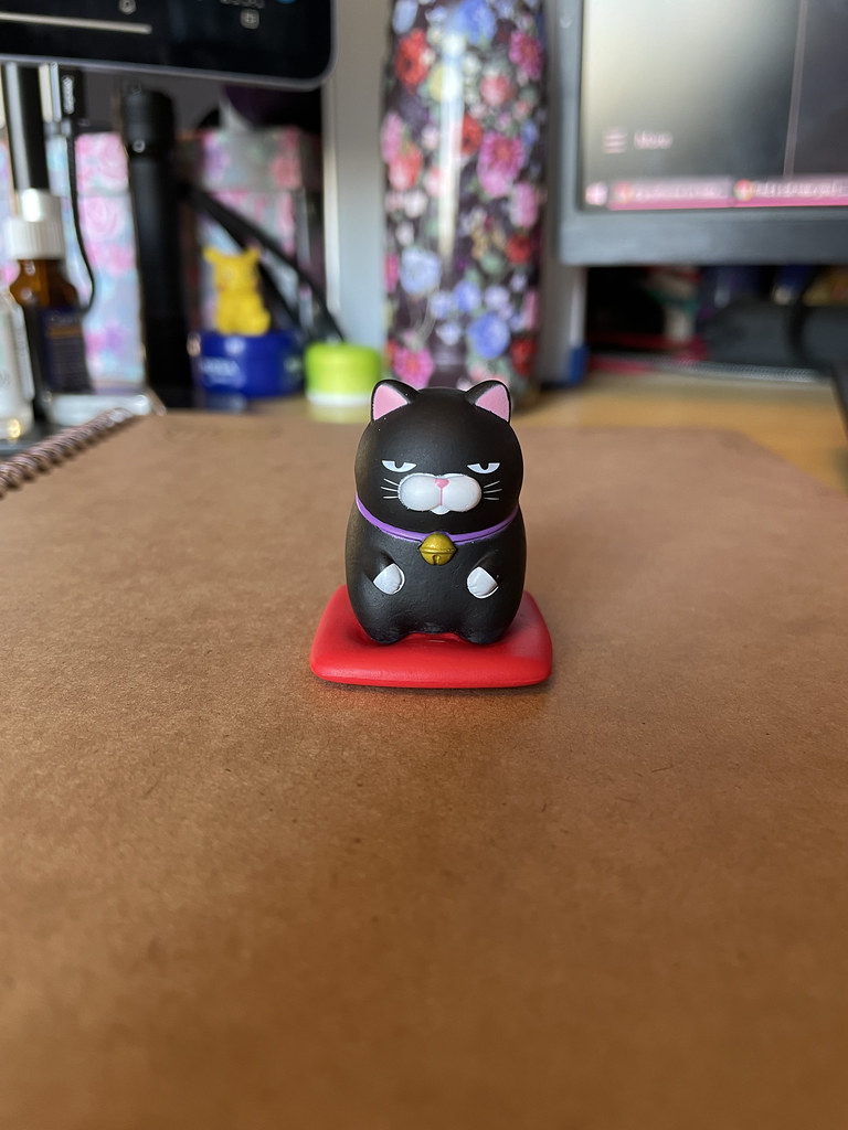 Grumpy black cat figurine on a red base amid a cluttered desk