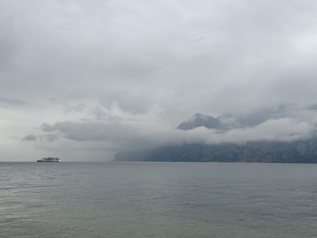 A boat is sailing on the Lake Garda under the grey clouds over the surrounding mountains, Malcesine, Veneto, Italy, October 2023
