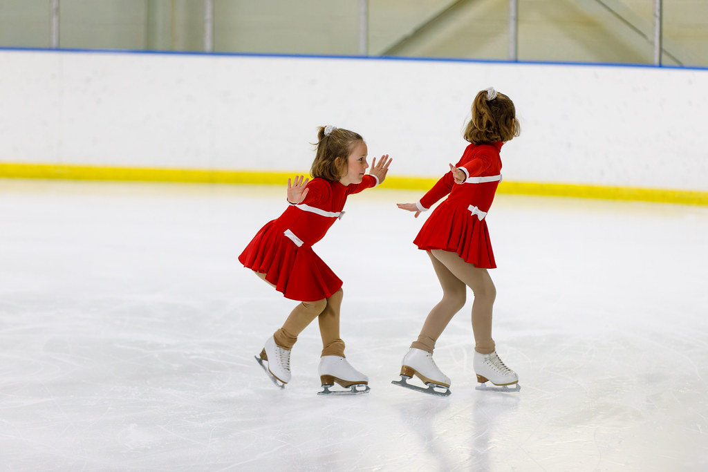 Two Young Figure Skaters in Red Perform a Synchronized Moment During a Winter Ice Show