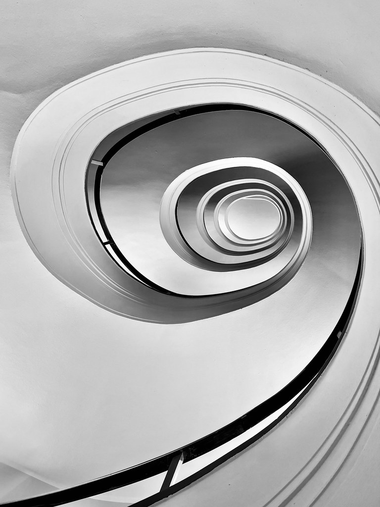 Spiral Ascent: monochrome architectural study of curved stair rails viewed from the base