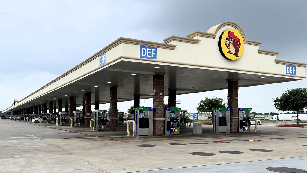 DEF-branded Buc-ee’s Travel Center, Katy, Texas: long beige canopy with brick columns sheltering fuel islands beneath the iconic beaver logo