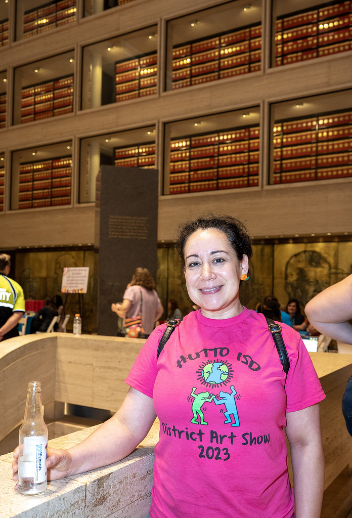 Smiling attendee in bright pink Hutto ISD District Art Show 2023 T-shirt at a library event