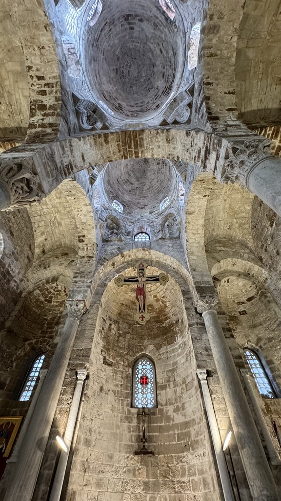 Vertical interior view of a medieval stone church with ribbed vaults, towering columns, and a crucifix suspended above the apse