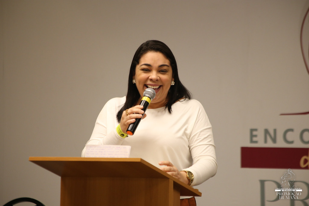 Apresentadora em palestra no Encontro Nacional de Promoção Humana, diante de púlpito de madeira com microfone