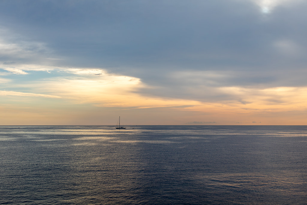 Sicilian Sunset: Lone Sailboat on a Calm Mediterranean Horizon