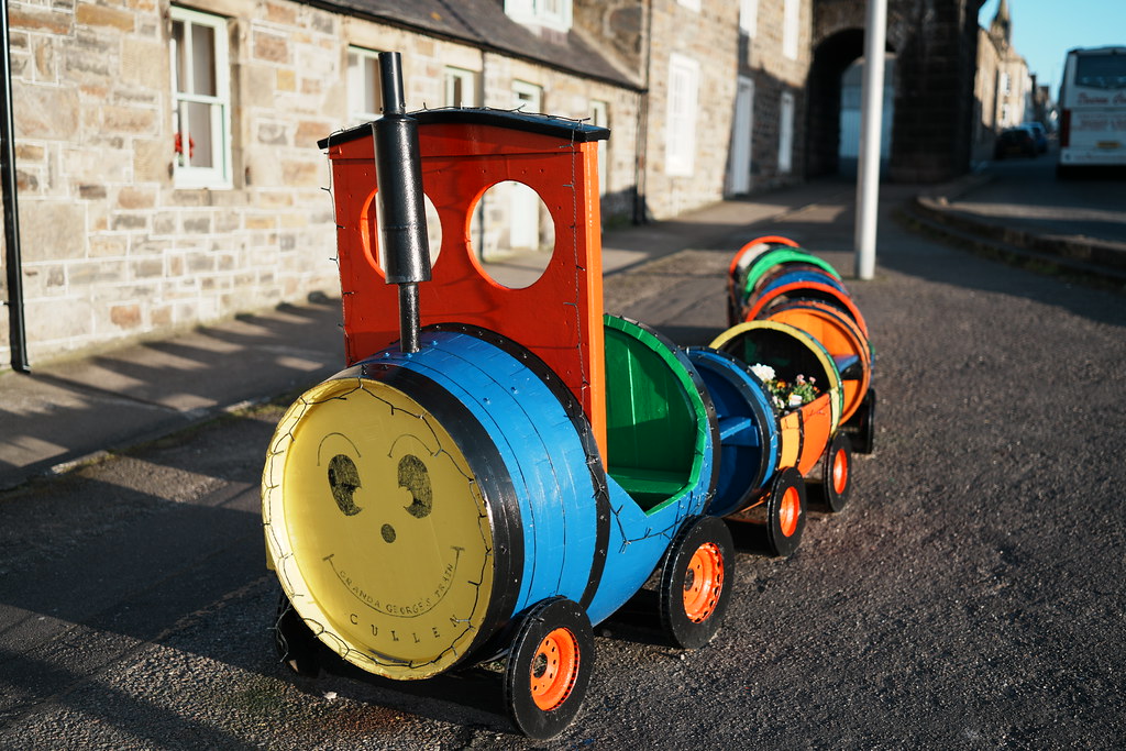Granda George's Train: vibrant recycled-tire locomotives lined up along a sunlit stone-town street