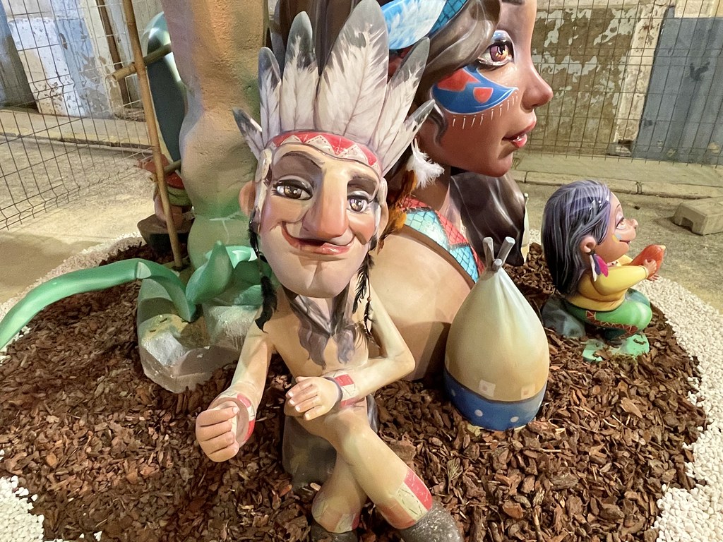 Colorful Fallas-style ninots group sculpture on a mulched display bed (Valencia-inspired)