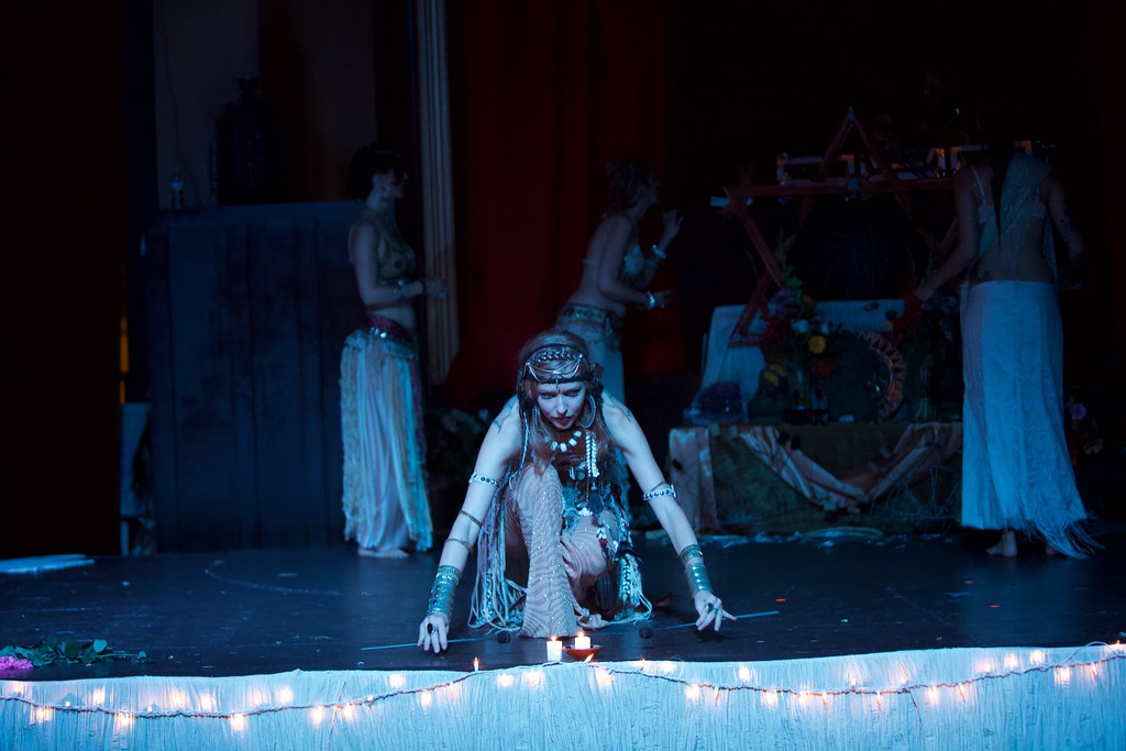 Ritual Dancer Kneels on Candled Stage Under Cool Blue Lighting; Background Performers Frame the Scene