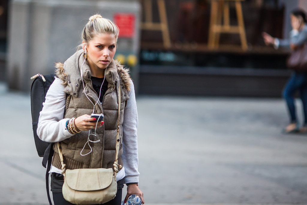 Solitary city stroll: a woman in a padded vest listens to music on a busy urban sidewalk
