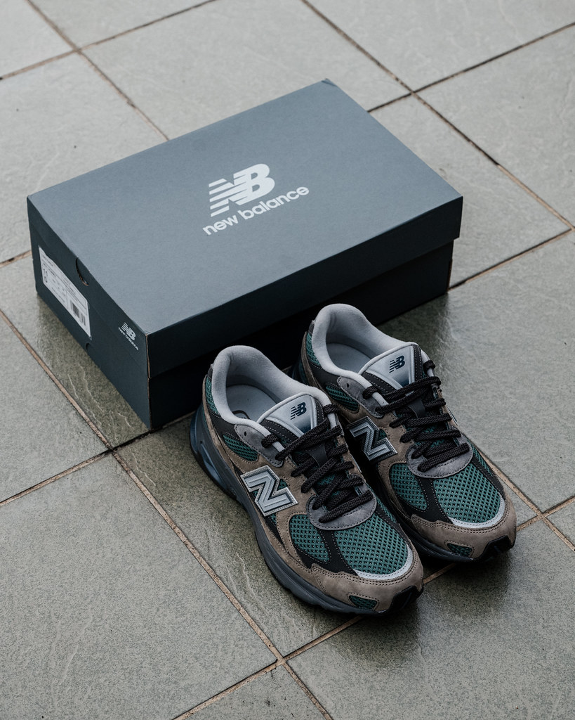 New Balance sneakers resting beside a blue-gray box on rain-darkened tile pavement